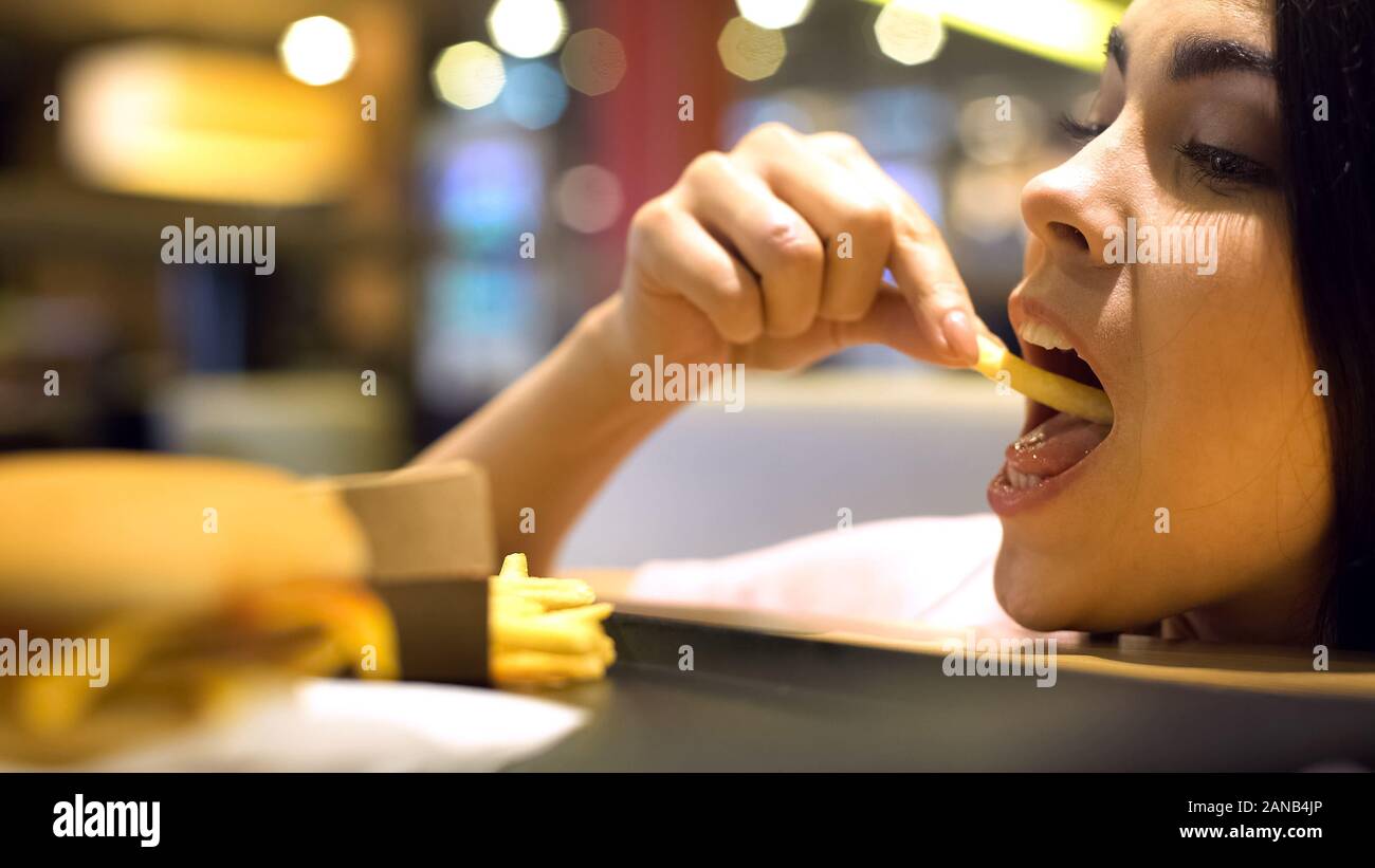 Young brunette woman eating french fried potatoes, junk food pleasure ...