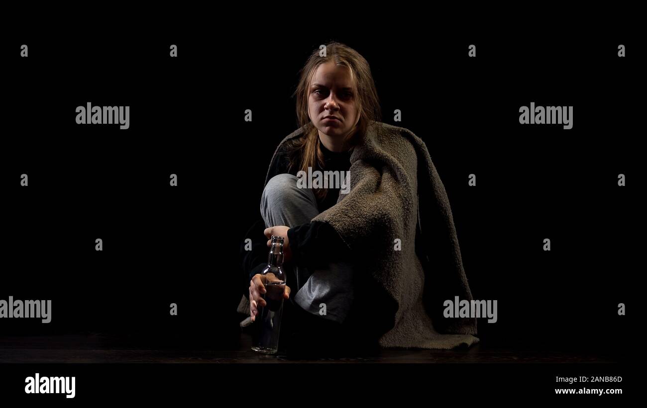 Depressed alcoholic female sitting in darkness with bottle of vodka ...