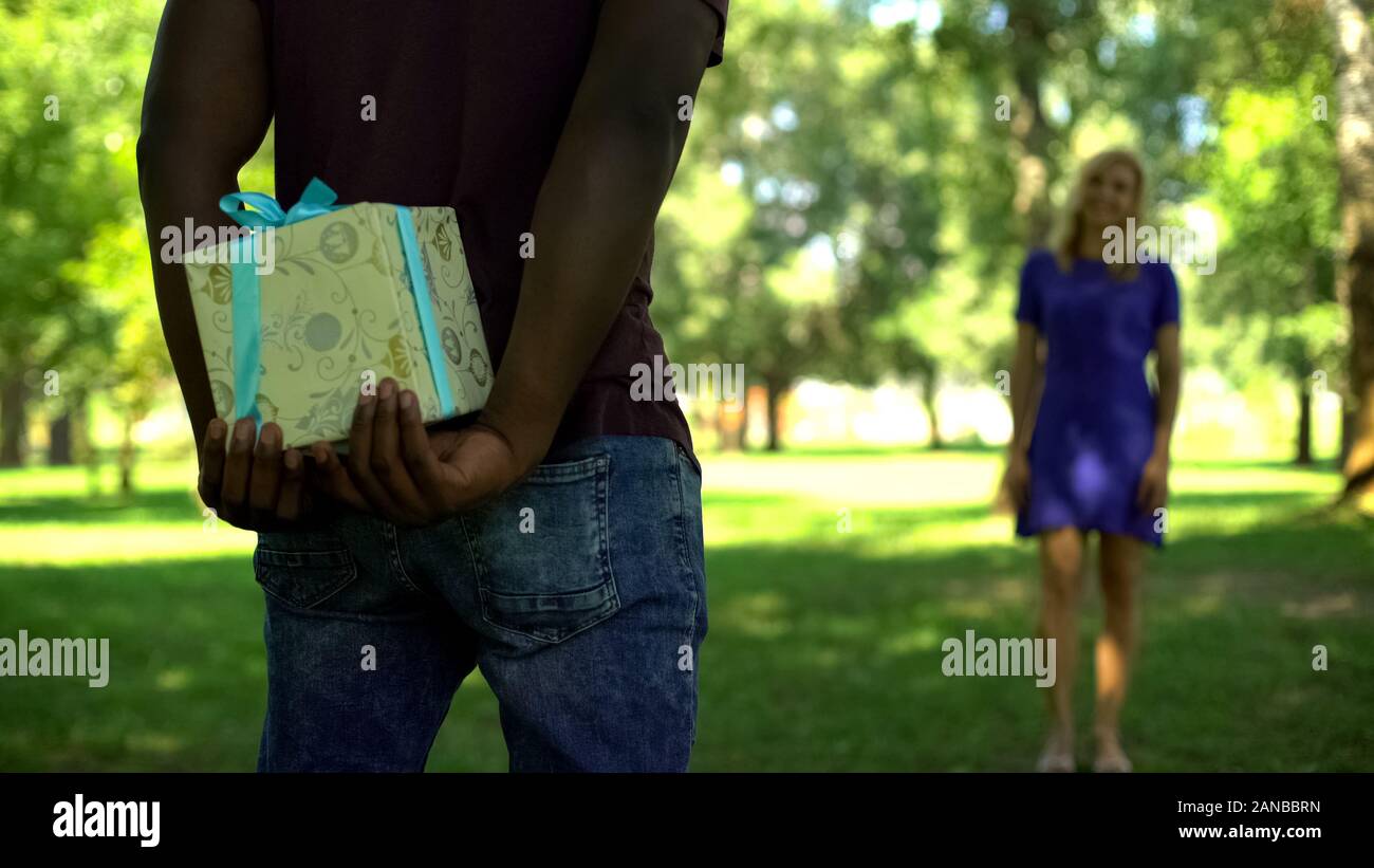 Afro american gentleman hiding present box behind back, celebrating ...