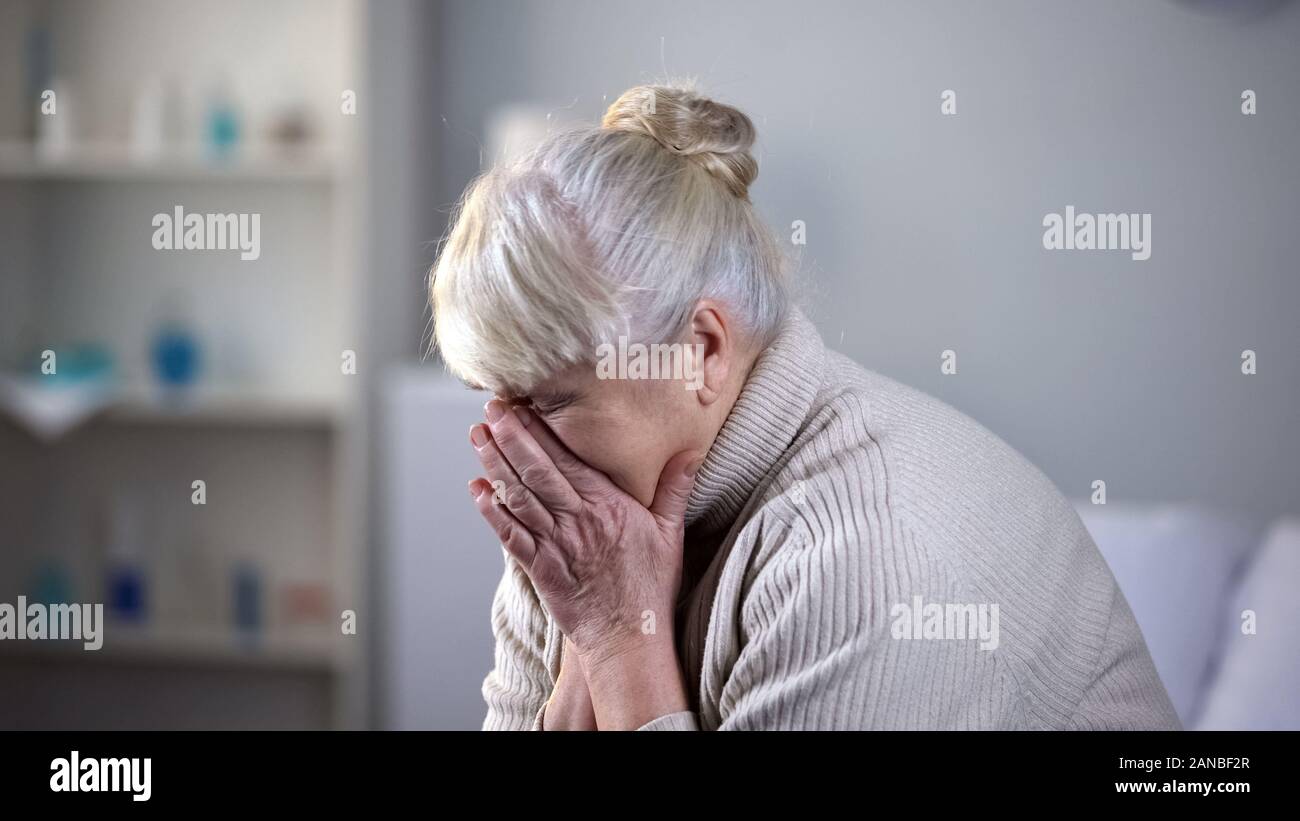 Unhappy elderly lady sitting alone in living room and deeply crying ...