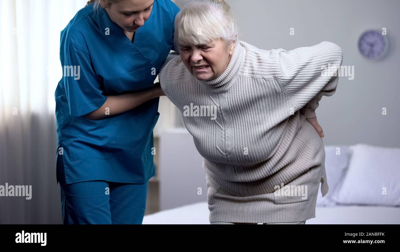 Nurse taking care about old lady suffering from lower back pain ...
