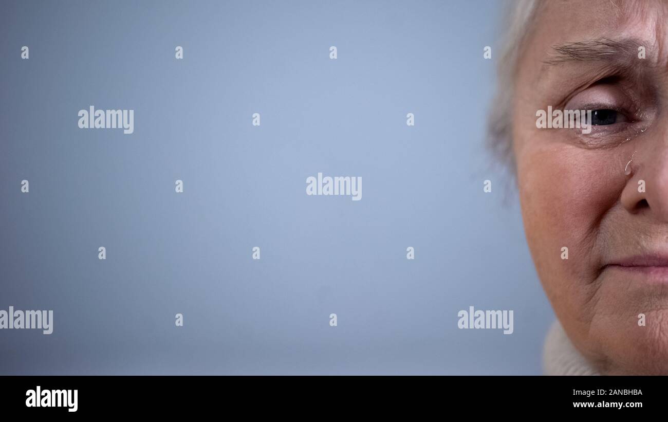 Half-face of upset crying elderly woman on grey background, poverty ...