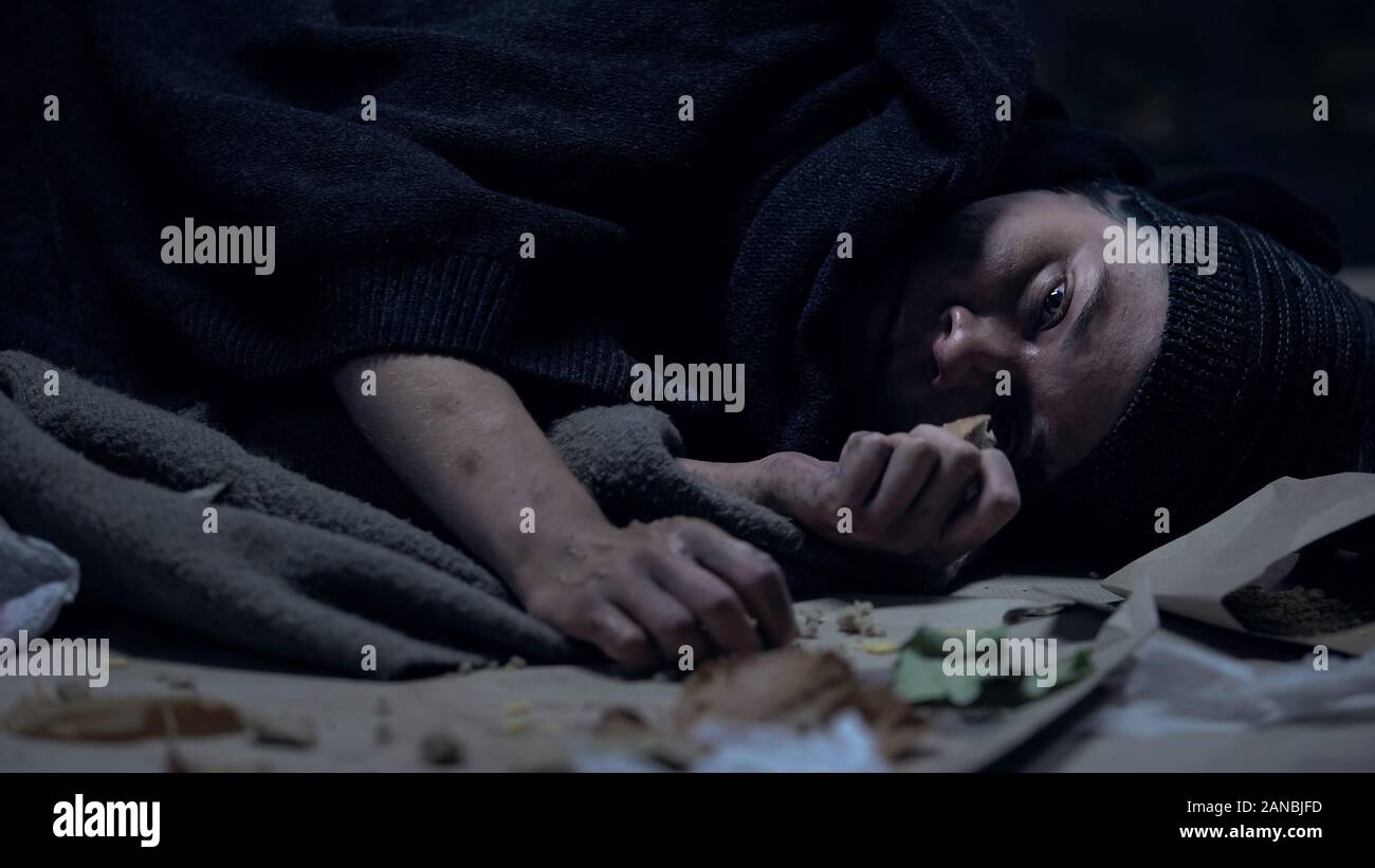 Sick hungry homeless person lying on street and eating last piece of ...