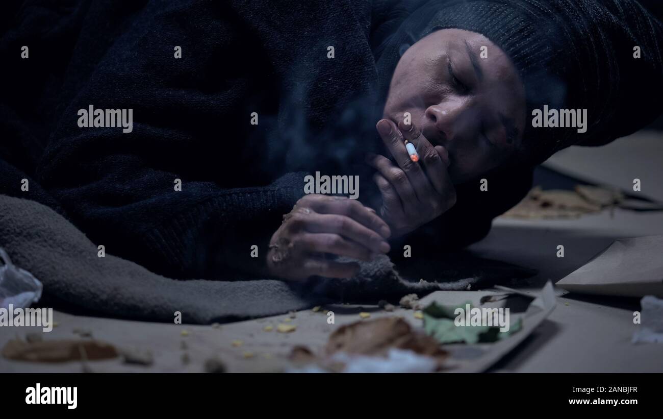 Homeless person smoking cigarette, lying on floor in dirty shelter ...
