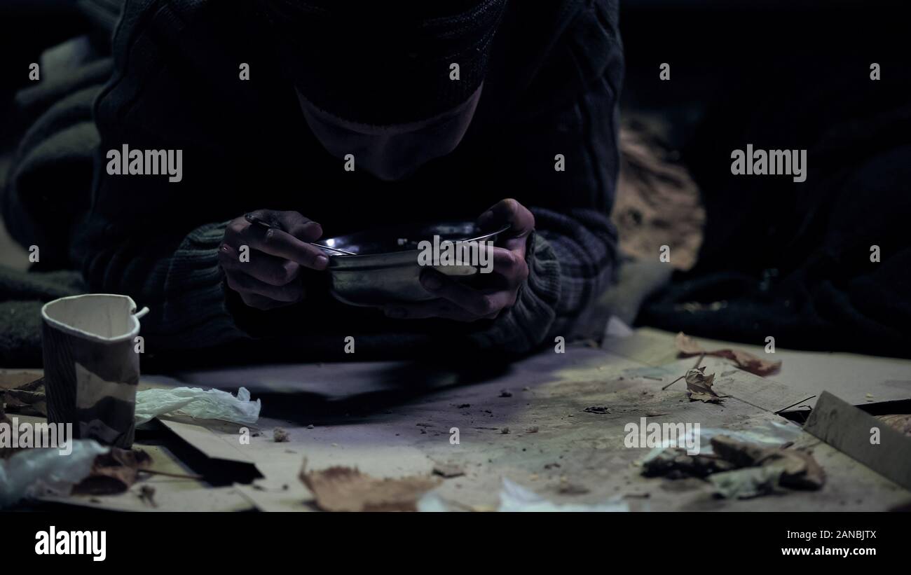 Hungry beggar eating from steel bowl sitting on dirty carton, street ...