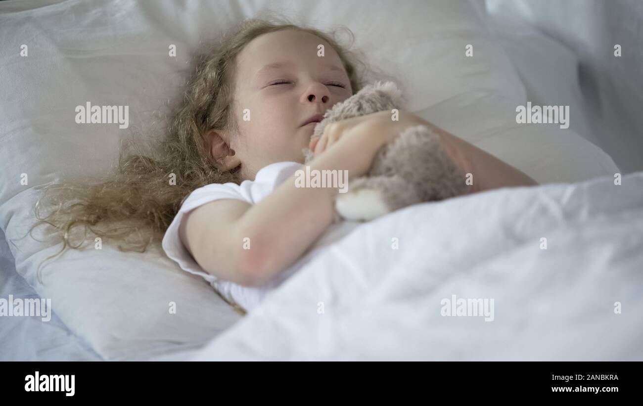 Lonely young girl lying in bed and hugging toy, unhappy child missing ...