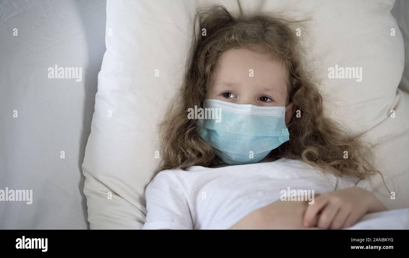 Sad child in medical face mask lying in bed, suffering rare disease ...
