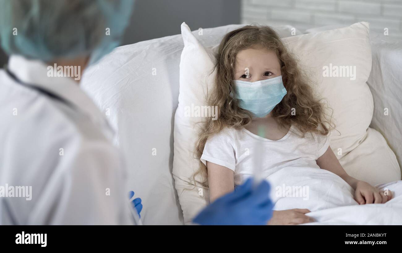 Nurse preparing to make injection to scared girl, wearing face mask ...