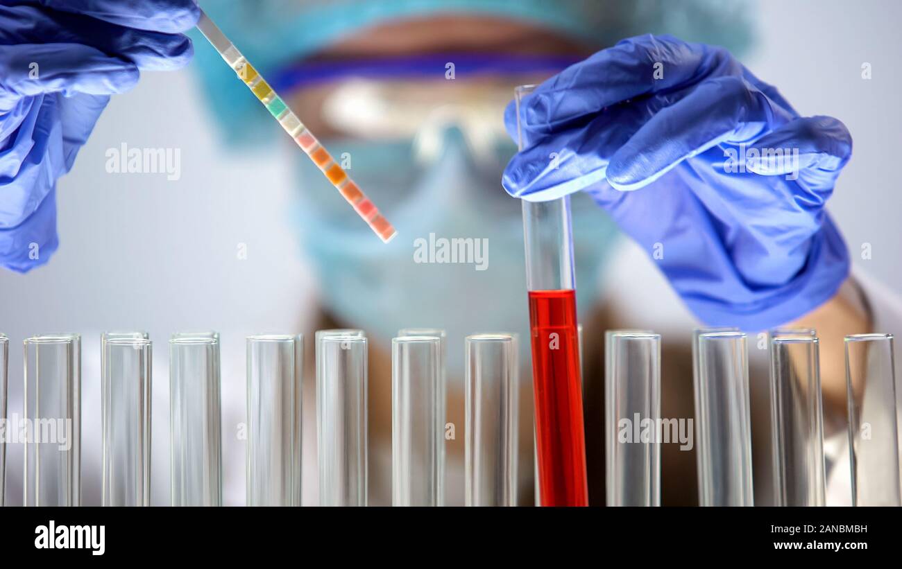 Researcher measuring pH level in red liquid substance with litmus paper ...