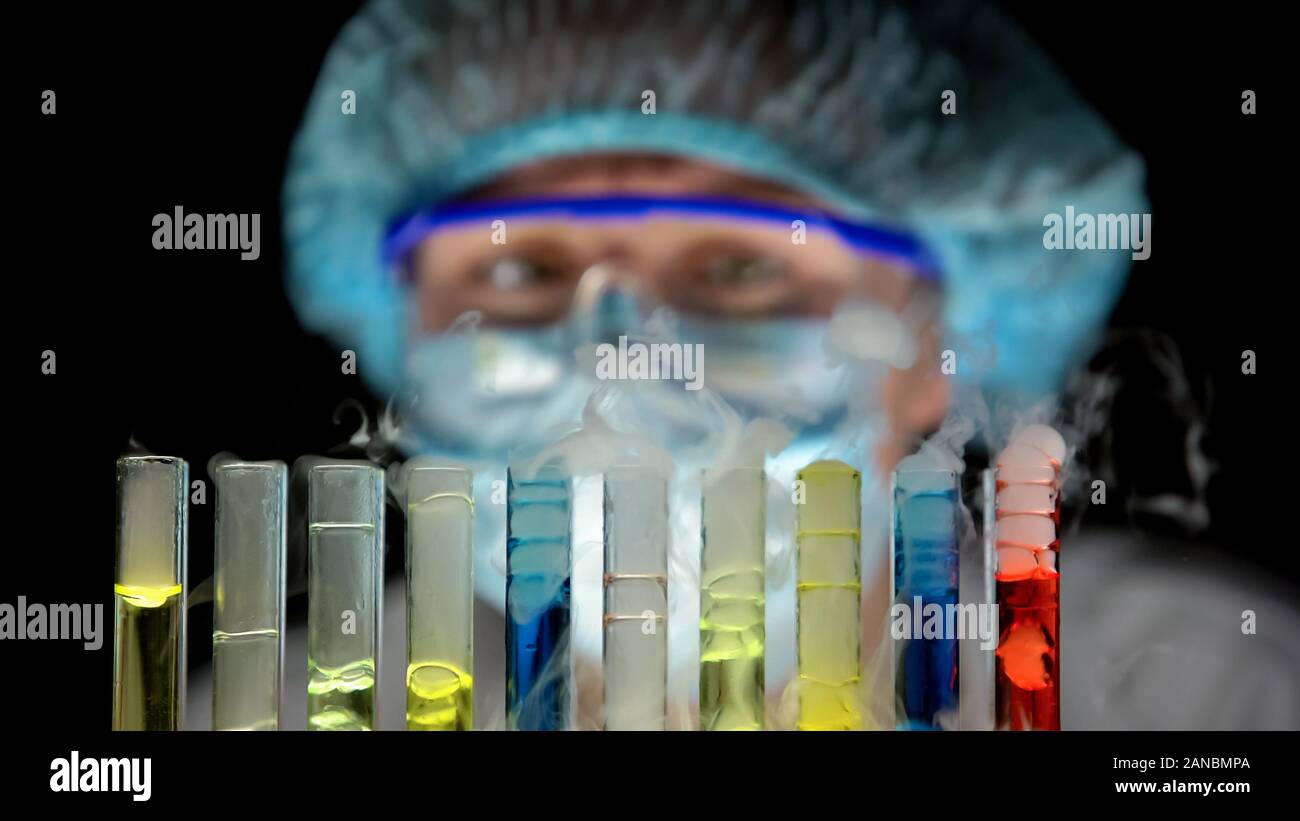 Scientist checking reaction in test tubes with multicolor liquids ...