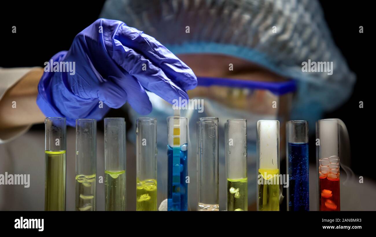 Scientist measuring acidity level in tube with blue liquid in dark ...