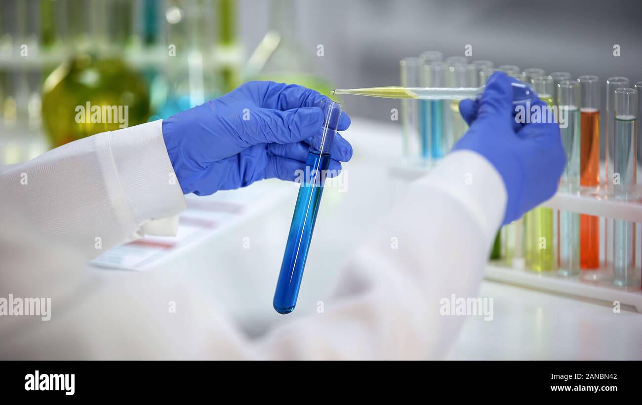 Lab assistant dripping yellow liquid in tube with blue chemical ...