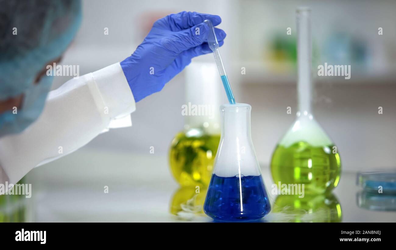 Chemist taking blue substance sample from flask, washing agent analysis ...