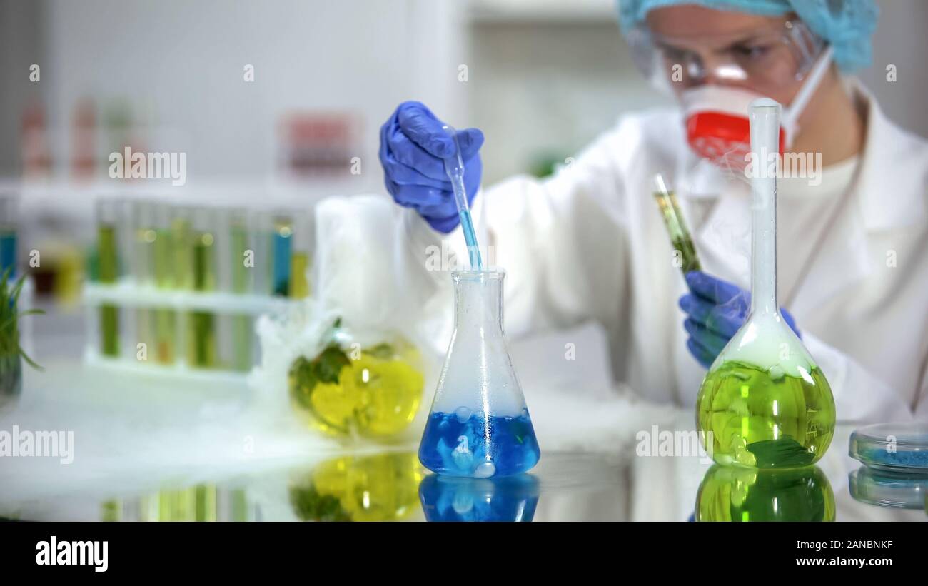 Lab researcher adding blue liquid substance in tube with green plant ...