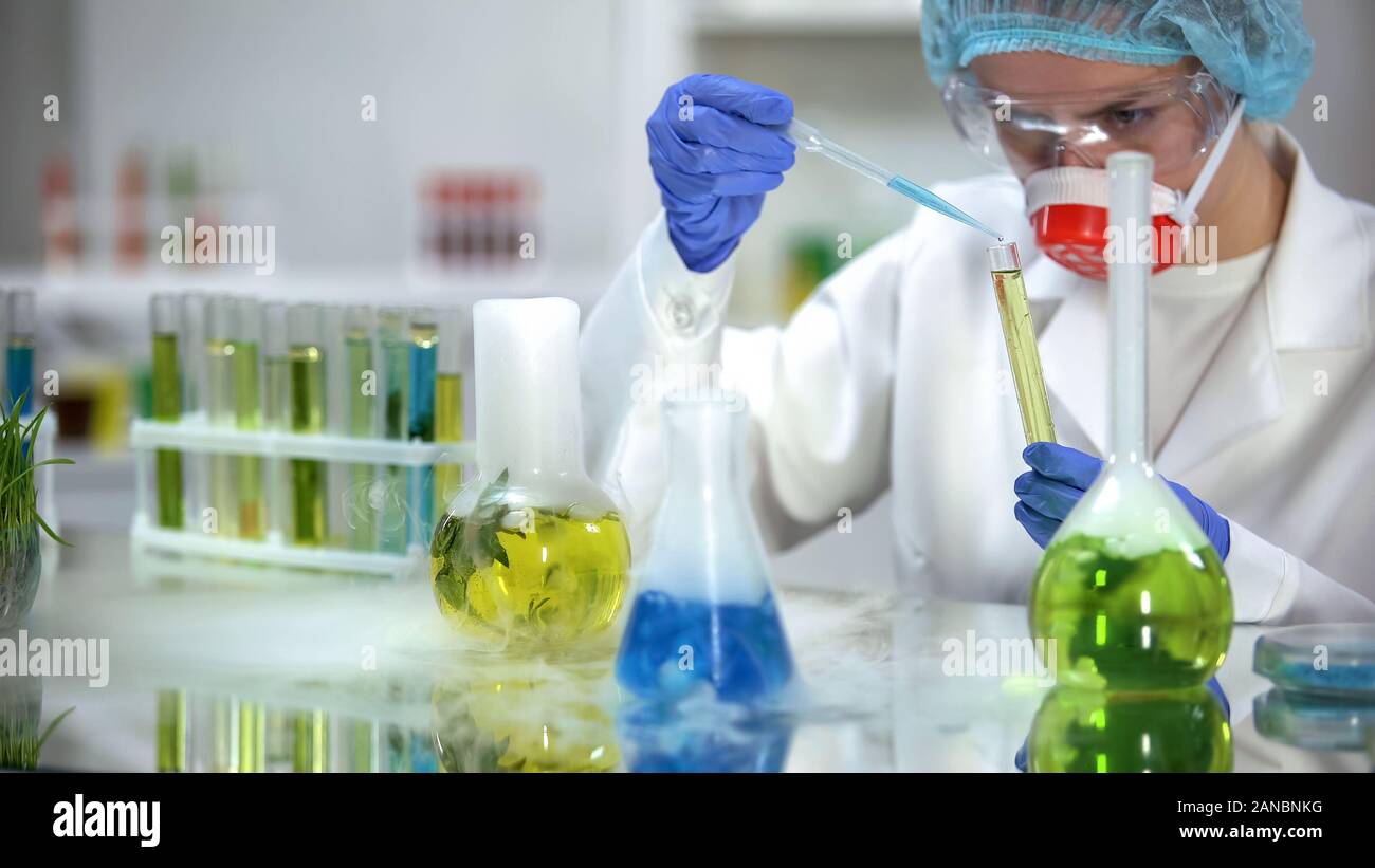 Chemist adding blue liquid in tube with yellow oily substance observing ...