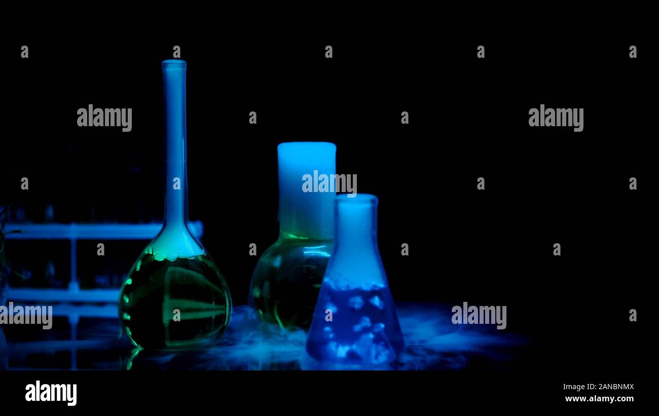 Laboratory flasks with chemical liquids emitting smoke under blue blue ...