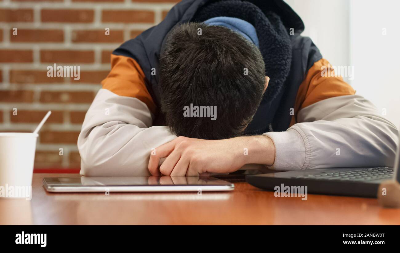 Tired male teenager sleeping on desk, laptop and tablet on table ...
