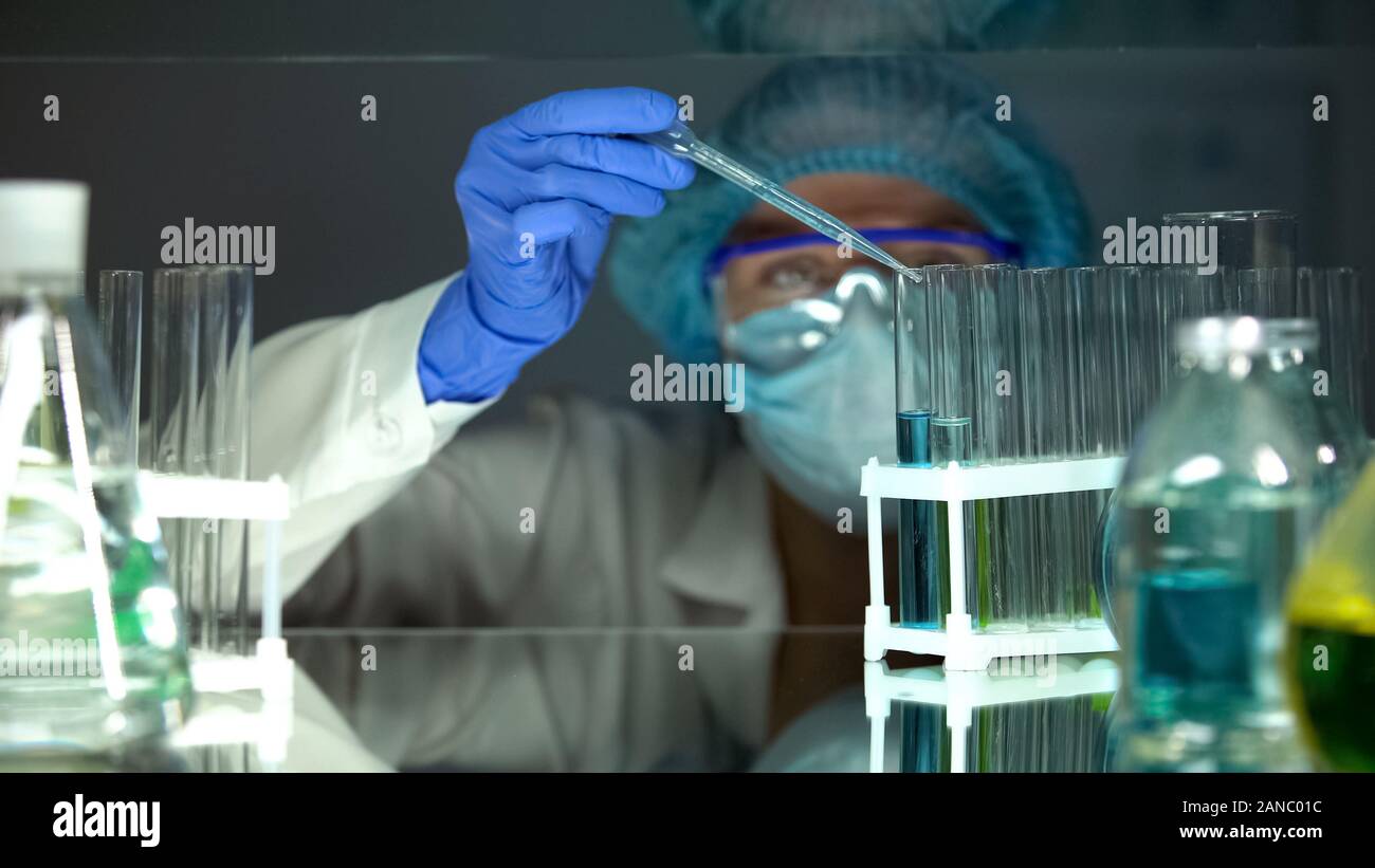 Scientist dripping chemical agent in tube with blue liquid conducting ...