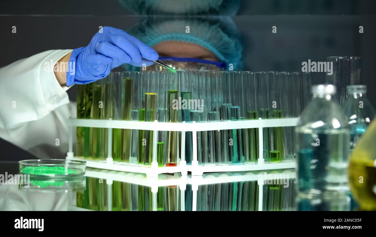 Researcher adding green powder in tube with yellow liquid and checking ...