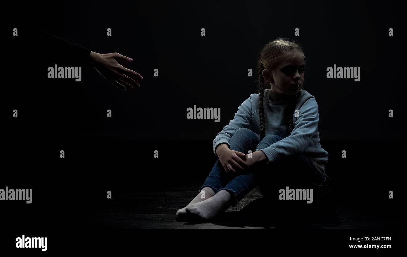 Distrustful little girl sitting in dark room refusing adult helping ...