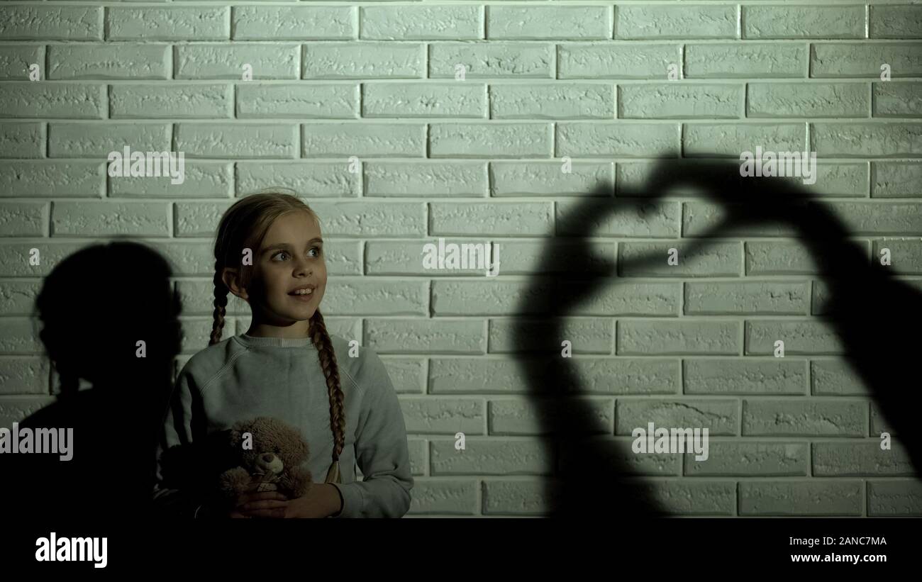 Girl looking at heart shadow on wall and hugging teddy bear, hope and ...
