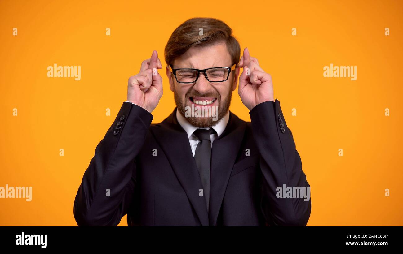 Nervous man in business suit crossing fingers for good luck, hoping to ...