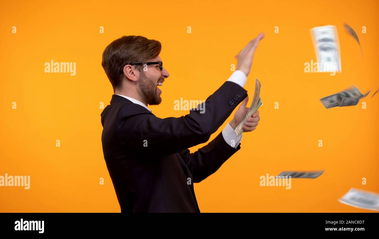 Positive businessman throwing dollar banknotes in air, spending money ...
