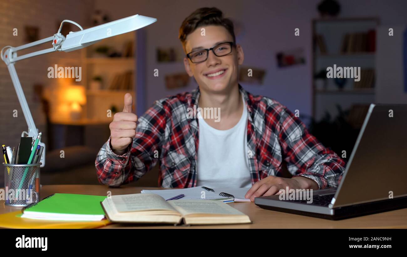 Intelligent student in glasses finishing homework showing thumbs-up to ...