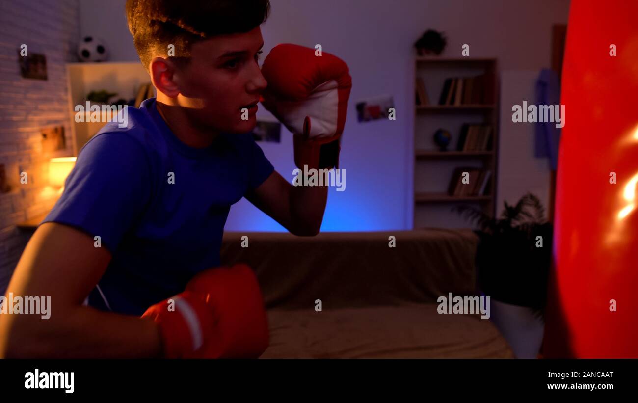 Teenager going for sport, punching boxing bag in his room, shadow ...