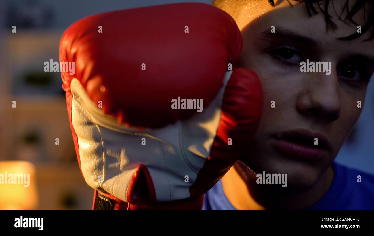 Exhausted teenager holding hand in boxing glove near face looking into ...