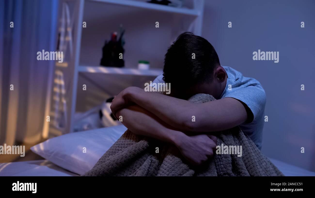Crying teenager sitting alone in evening bedroom, bullying victim ...
