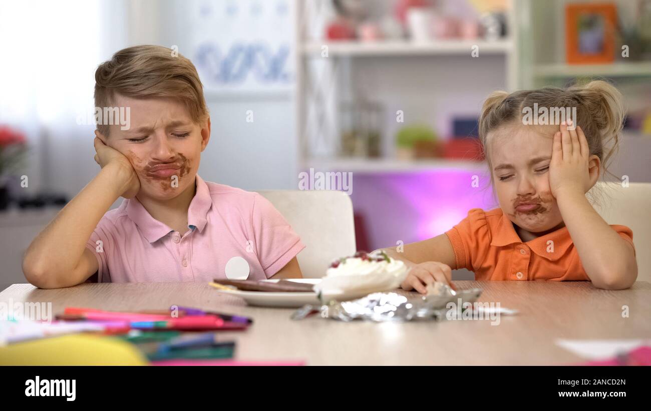 Two children smeared with chocolate sitting at table, stomach pain ...