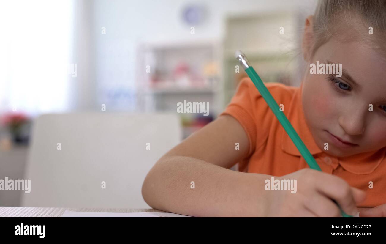 Studious little girl writing with pencil at home table, childhood ...