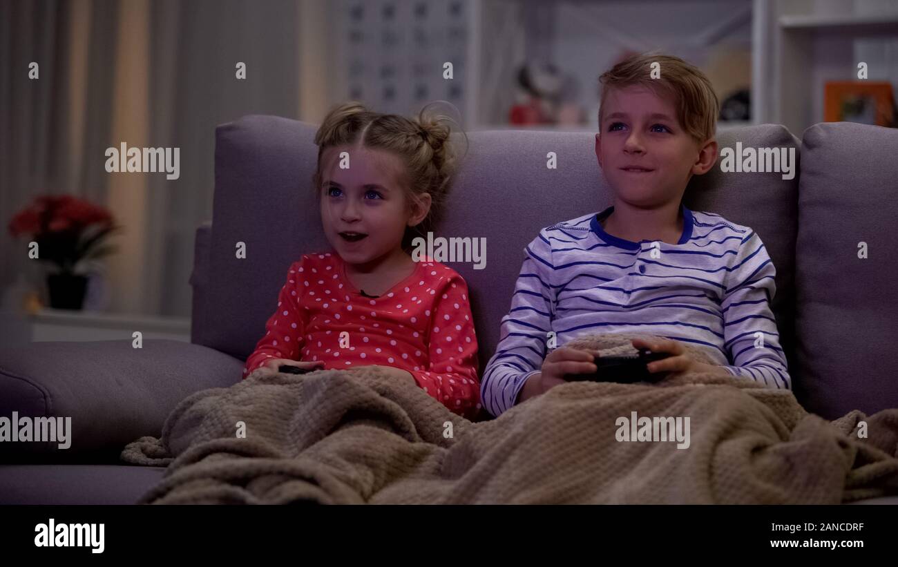 Siblings covered with plaid enjoying video game, playing at night ...
