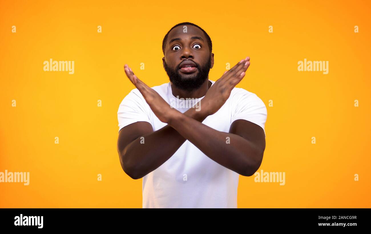 Afro-american young man showing stop sign by hands on yellow background ...