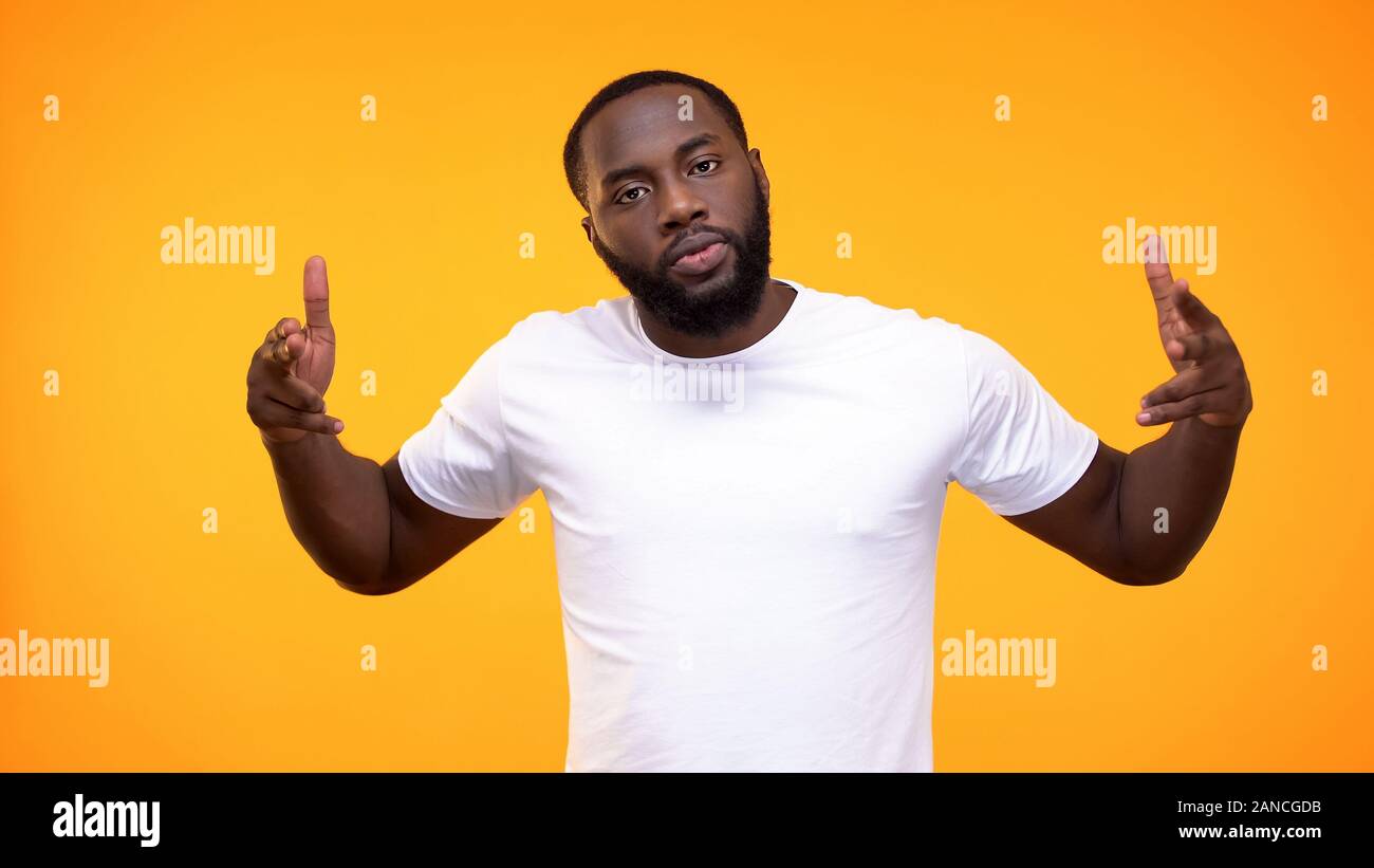Angry black male pointing finger guns on camera on yellow background ...