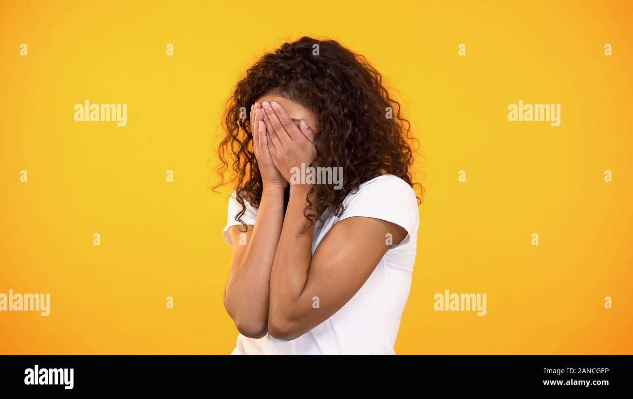 Scared female covering face by hands on bright background, frightened ...