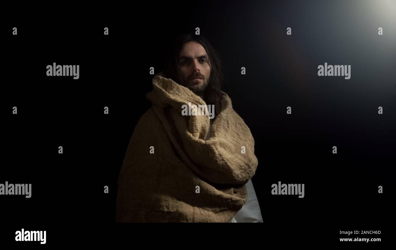 Male in robe standing in darkness and looking into camera, god blessing ...