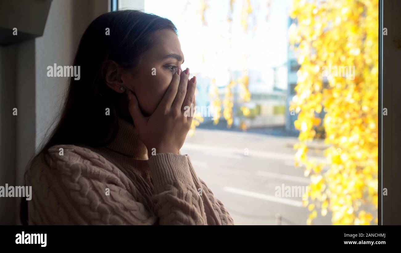 Crying lady looking through window, afraid of going outdoors ...