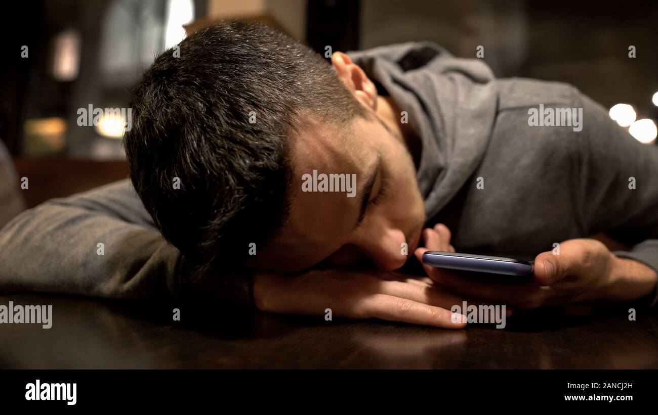 Tired man sleeping on table in restaurant, holding smartphone, busy ...