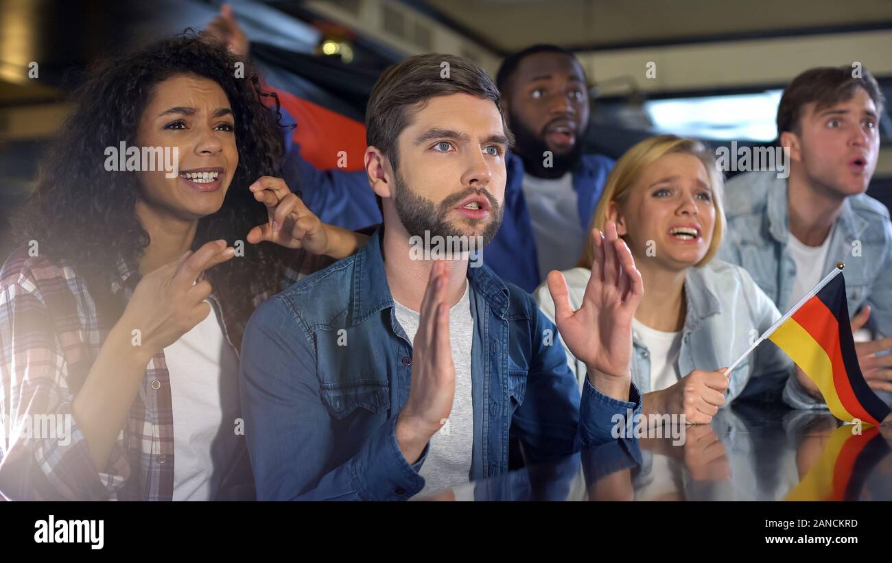 Nervous supporters waving German flag, watching sports program in bar ...