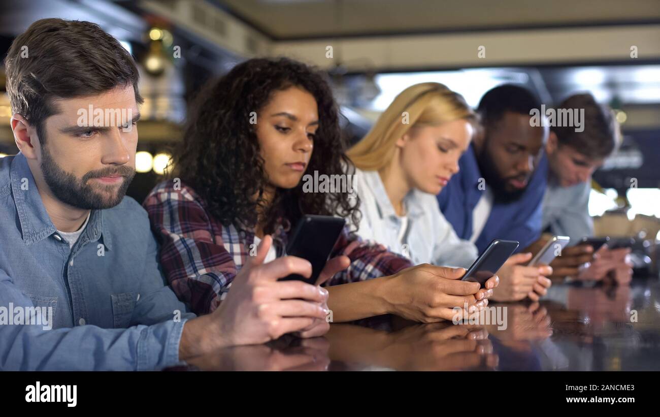 Multi-racial friends scrolling smartphones ignoring each other, gadget ...