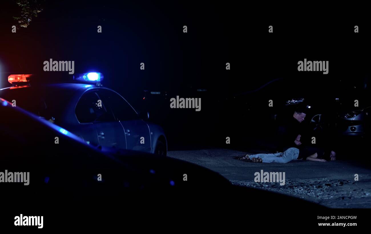 Cop getting out from patrol car and checking victim of crime lying on ...