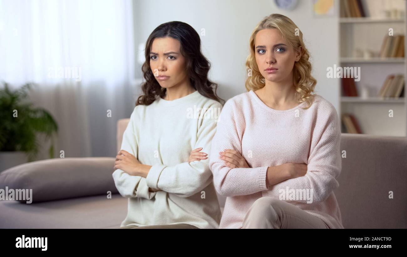 Two offended women sitting on sofa with hands crossed, conflict between ...