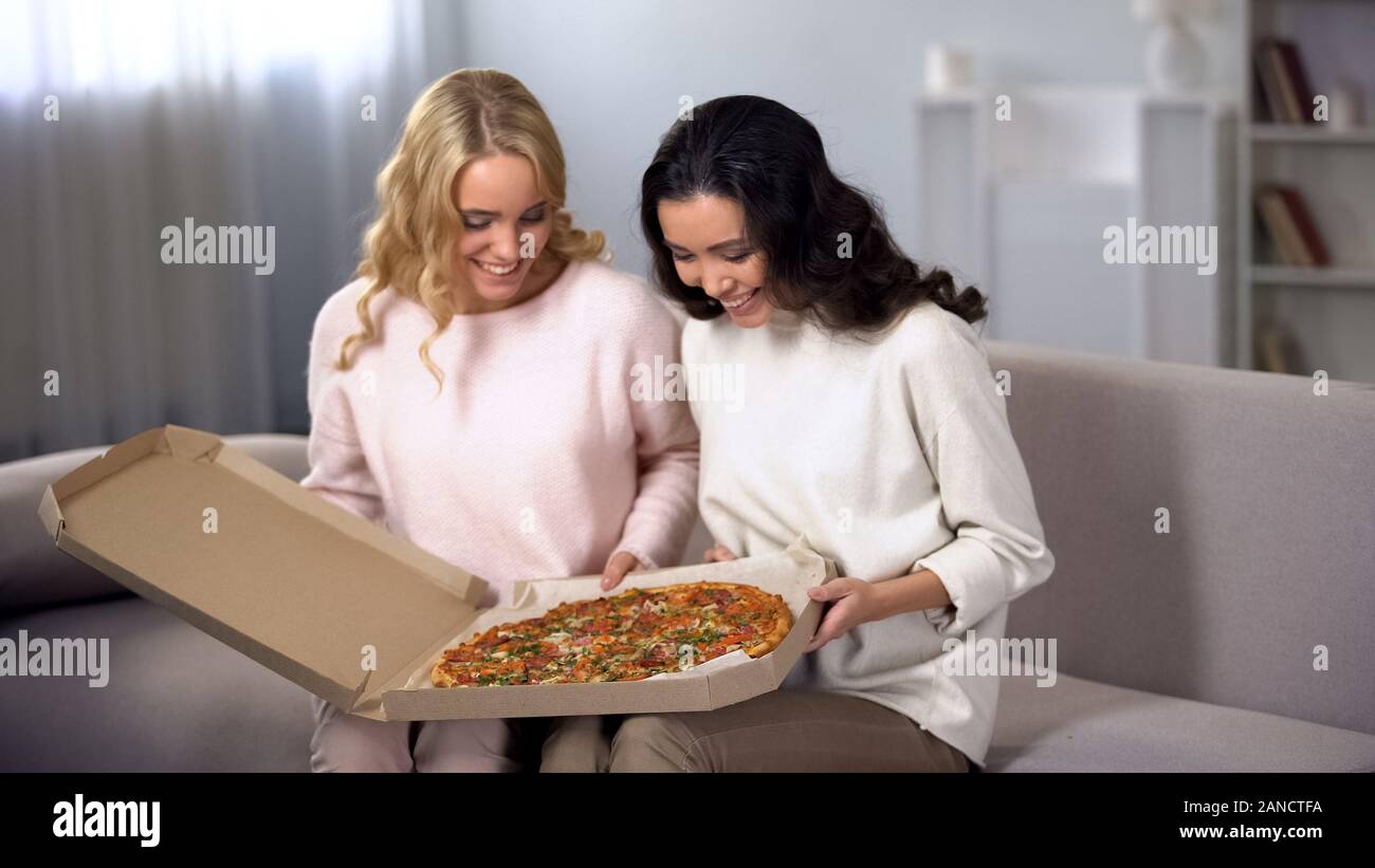 Two smiling female friends having pizza on launch, food delivery ...