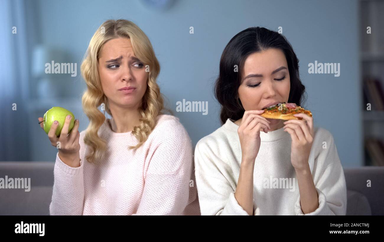 Lady eating pizza while female friend enjoying green apple, healthy ...