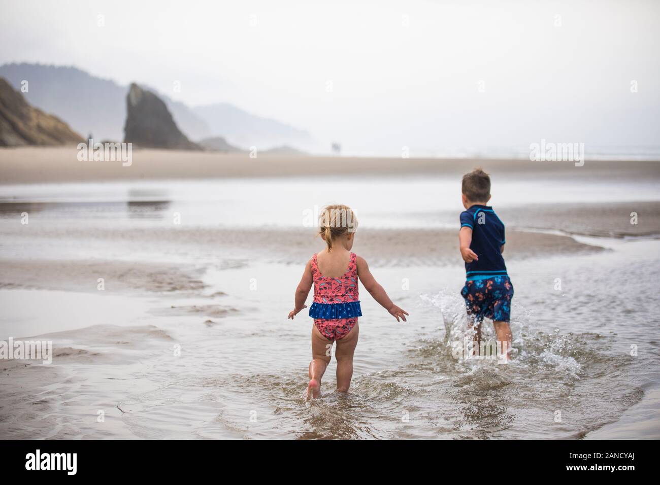 Brother and sister run through shallow water at the beach Stock Photo ...