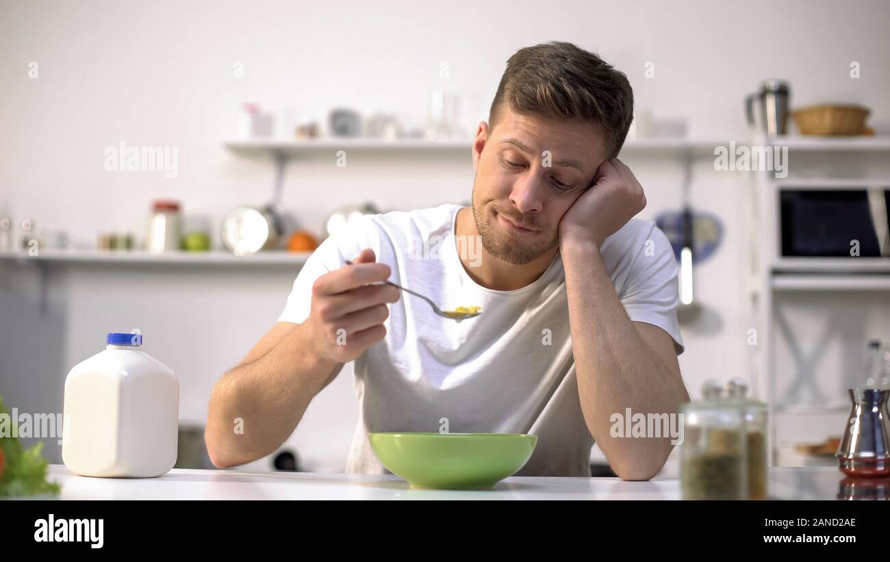 Upset single man eating tasteless cereals for breakfast, lack of ...