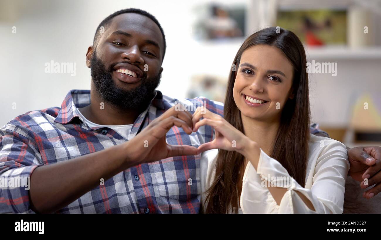Cheerful multiracial couple showing heart sign made with hands at ...