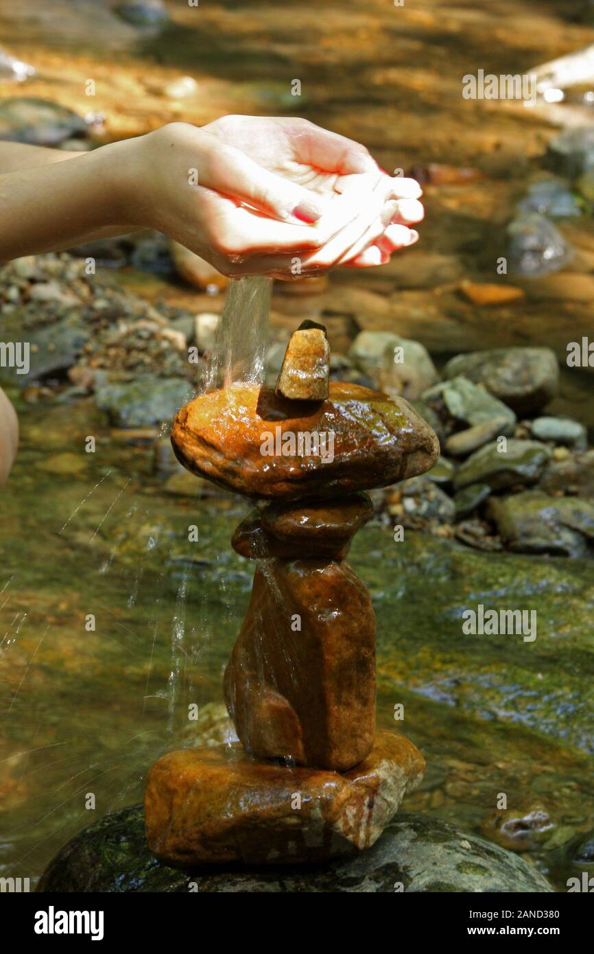 Young woman pouring water over a rock tower by the river Stock Photo ...